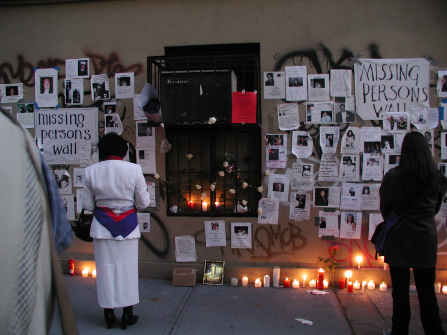 People looking at a missing persons wall - Village Preservation