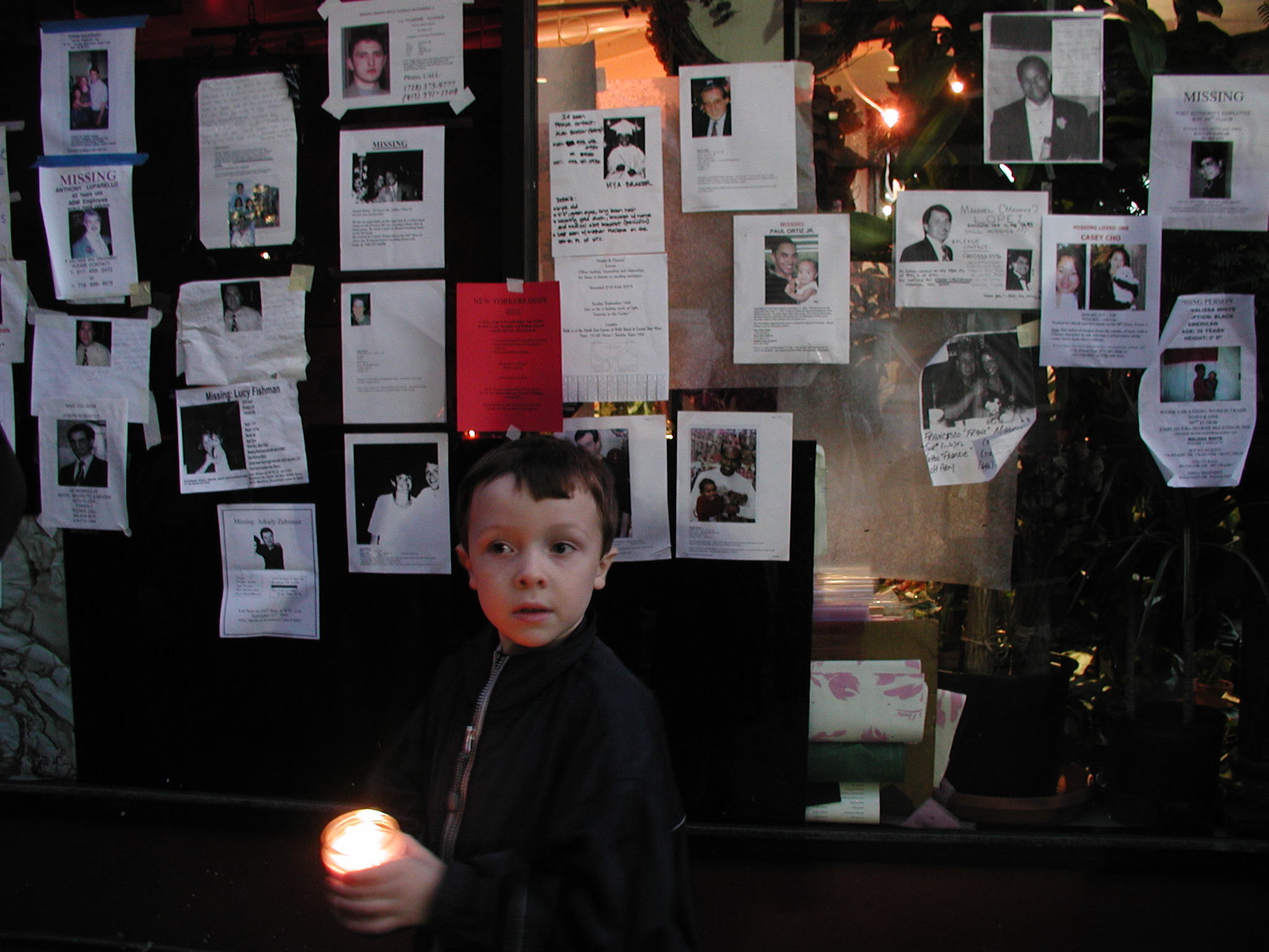 Child holds candle at missing persons wall - Village Preservation
